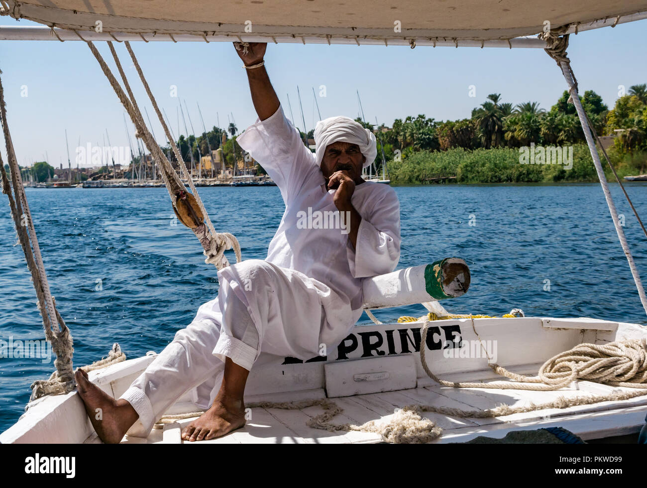Old Egyptian man in white jellabiya and turban steering rudder of ...