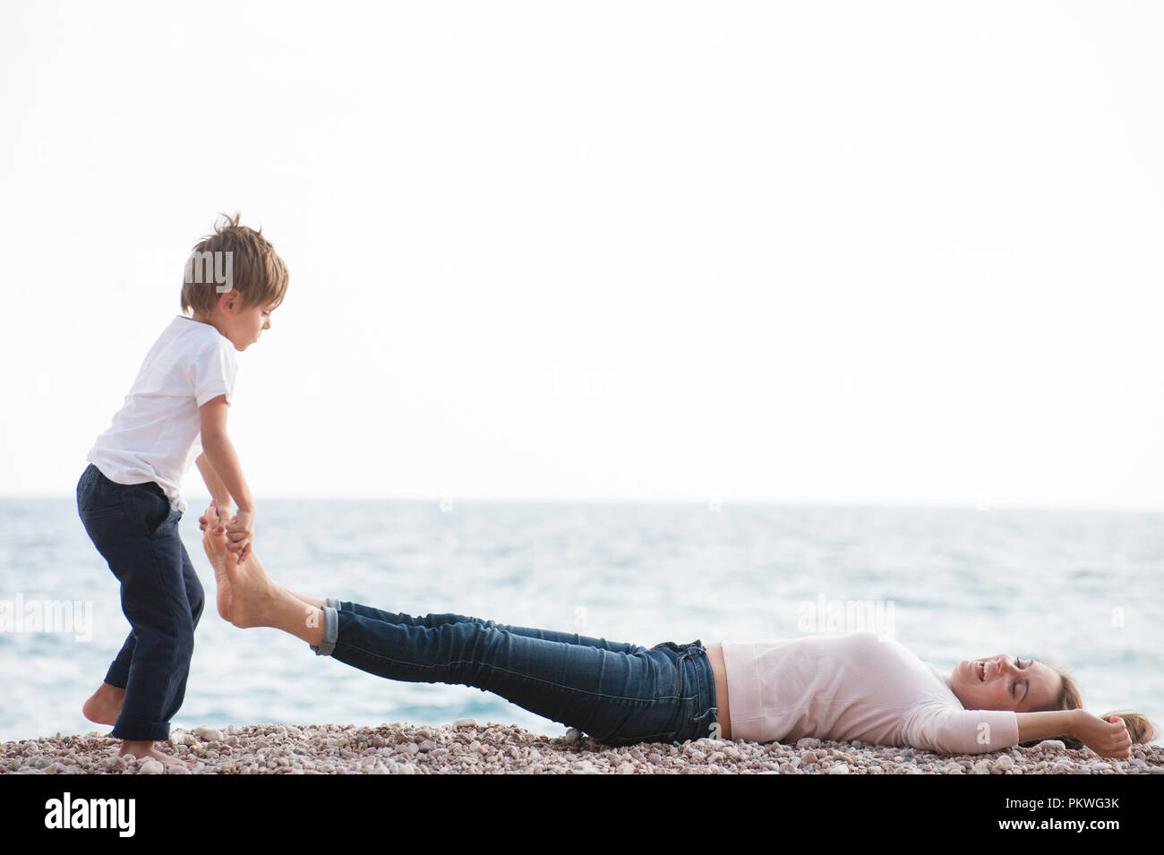 funny kid lifting happy mother legs playing on ocean shore in autumn ...