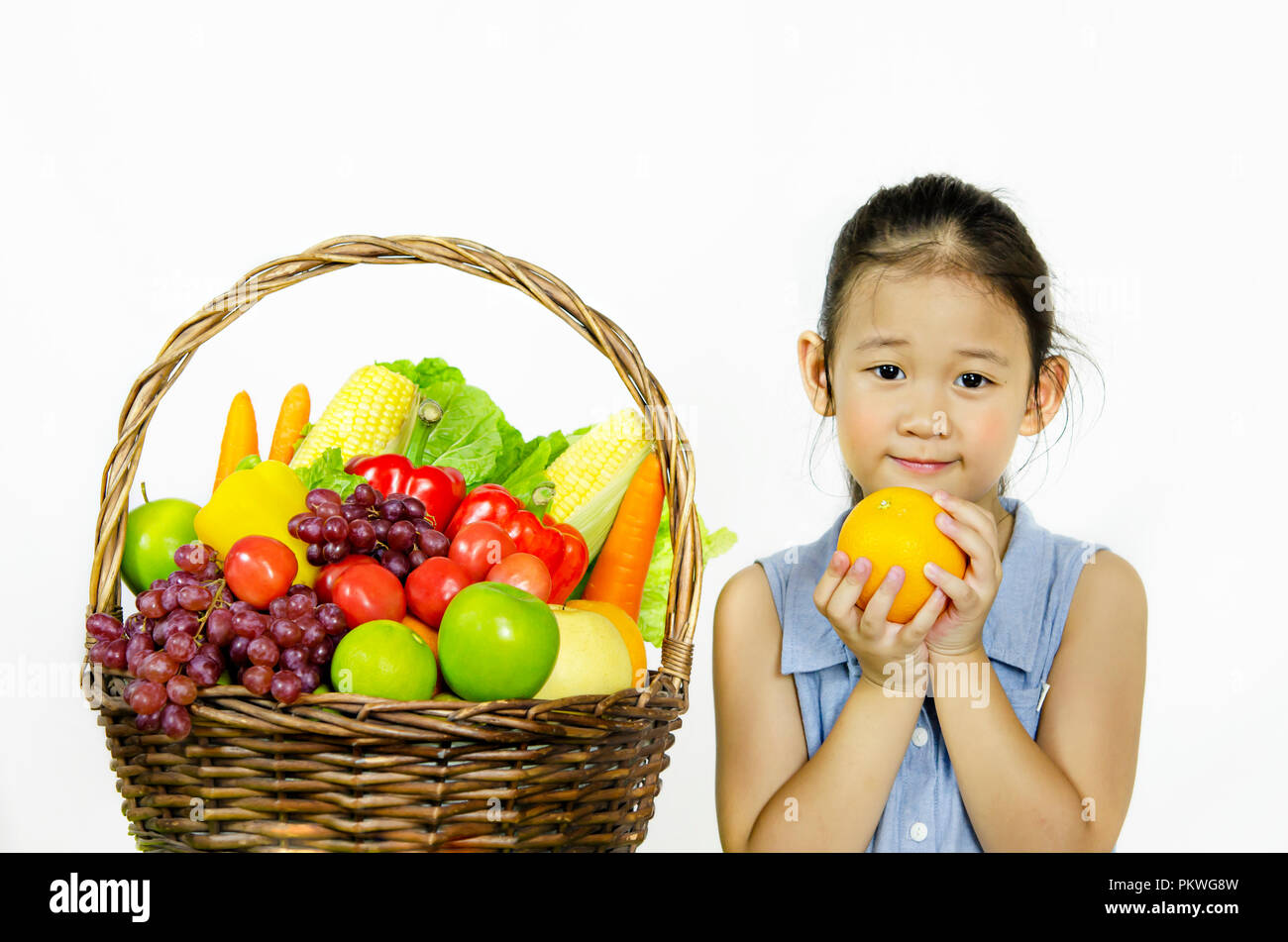 Smiling asian little girl with fruits and vegetables in basket over ...