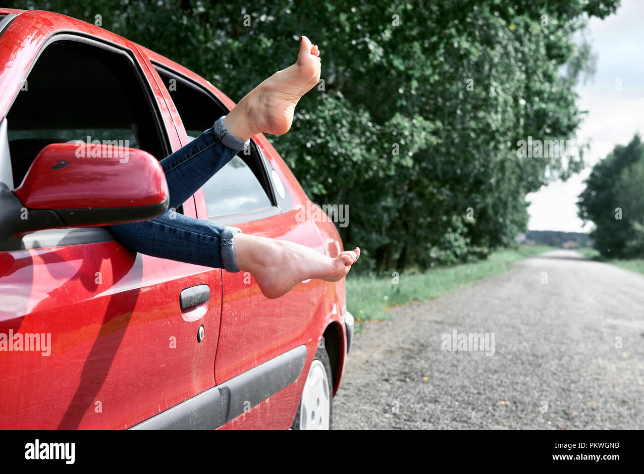 young woman driver resting in a red car, put her feet on the car window ...