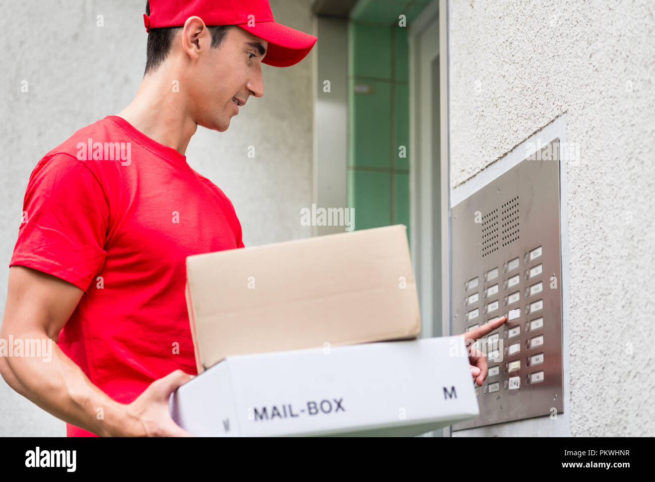 Delivery man carrying mail packages using the intercom Stock Photo - Alamy