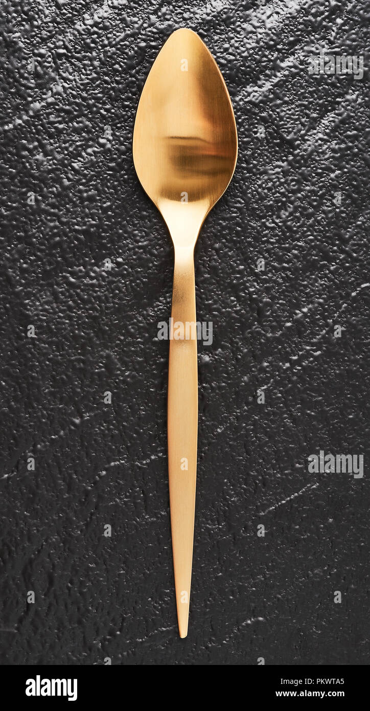 Flat lay of golden spoon on black extrusive volcanic rock effect ...