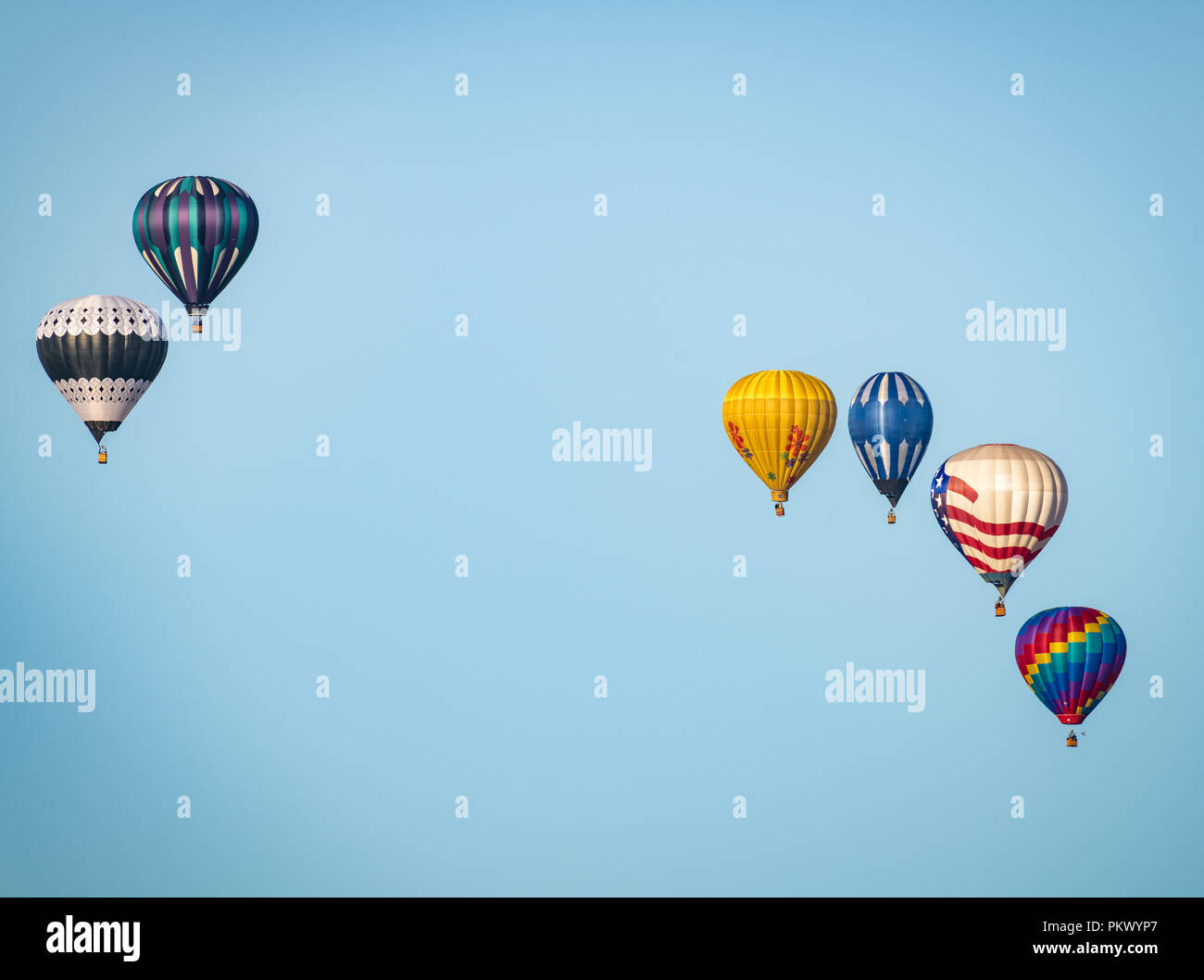 Balloons begin to seperate as they float above the land with a blue sky ...