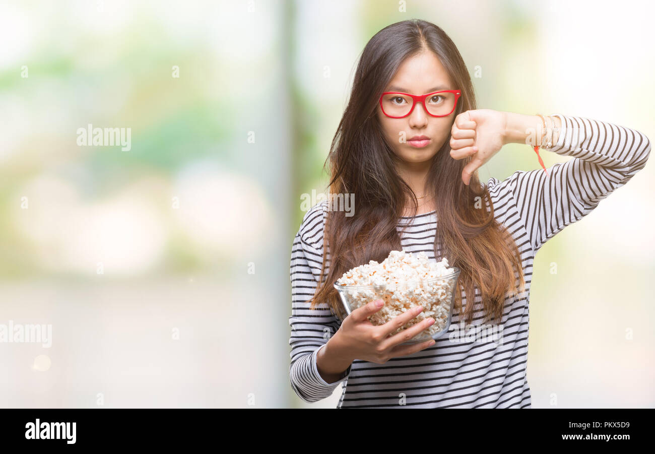 Young asian woman eating popcorn over isolated background with angry ...