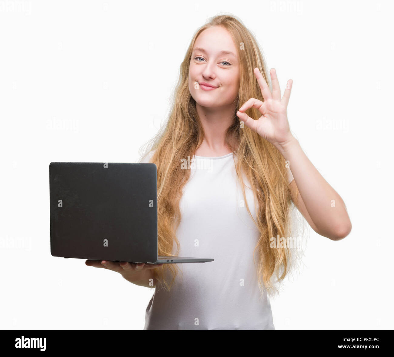 Blonde teenager woman using computer laptop doing ok sign with fingers ...