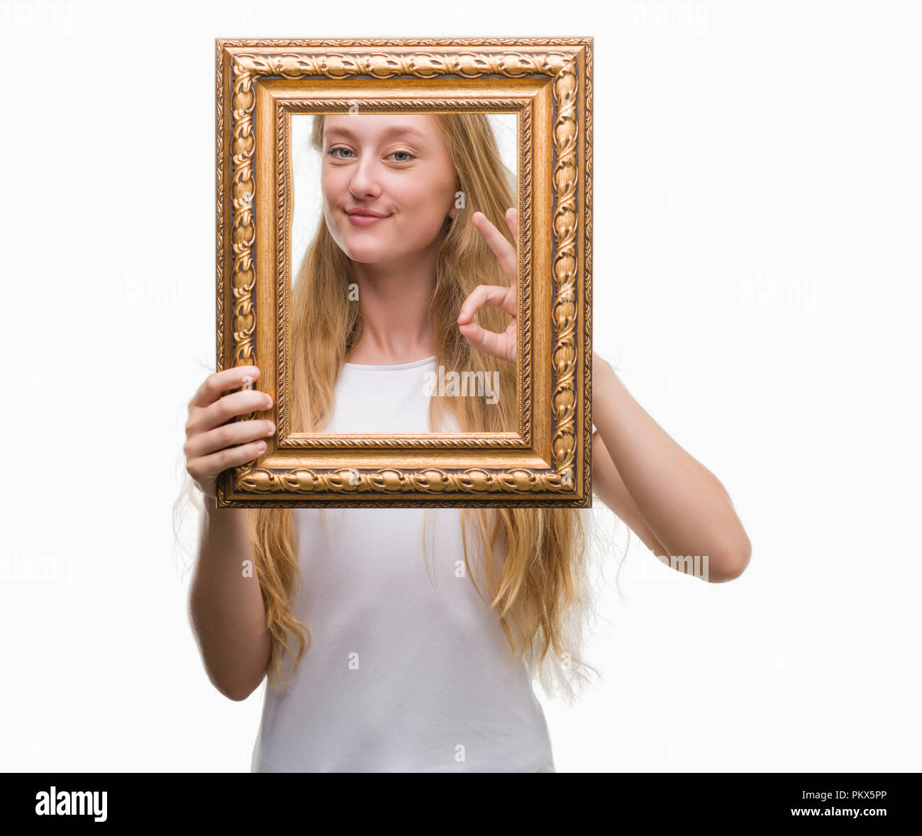 Blonde teenager woman holding vintage frame art doing ok sign with ...