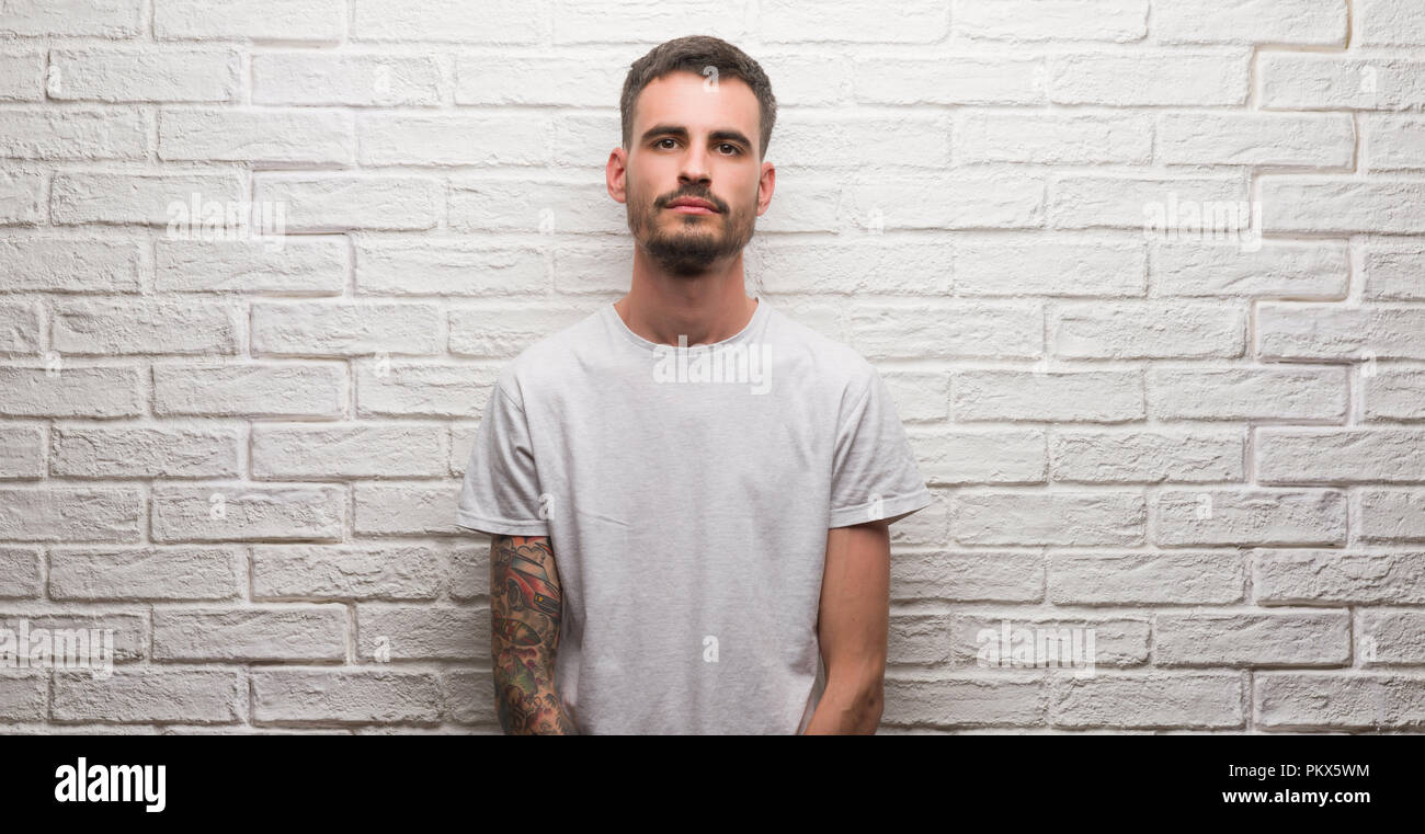 Young adult man standing over white brick wall with a confident ...