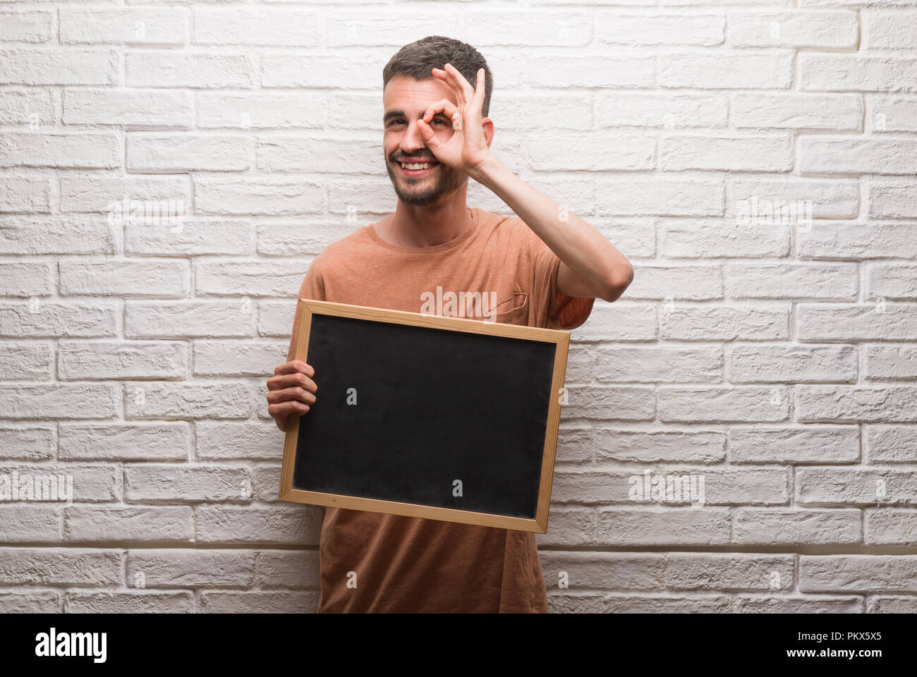Young adult man over brick wall holding blackboard with happy face ...