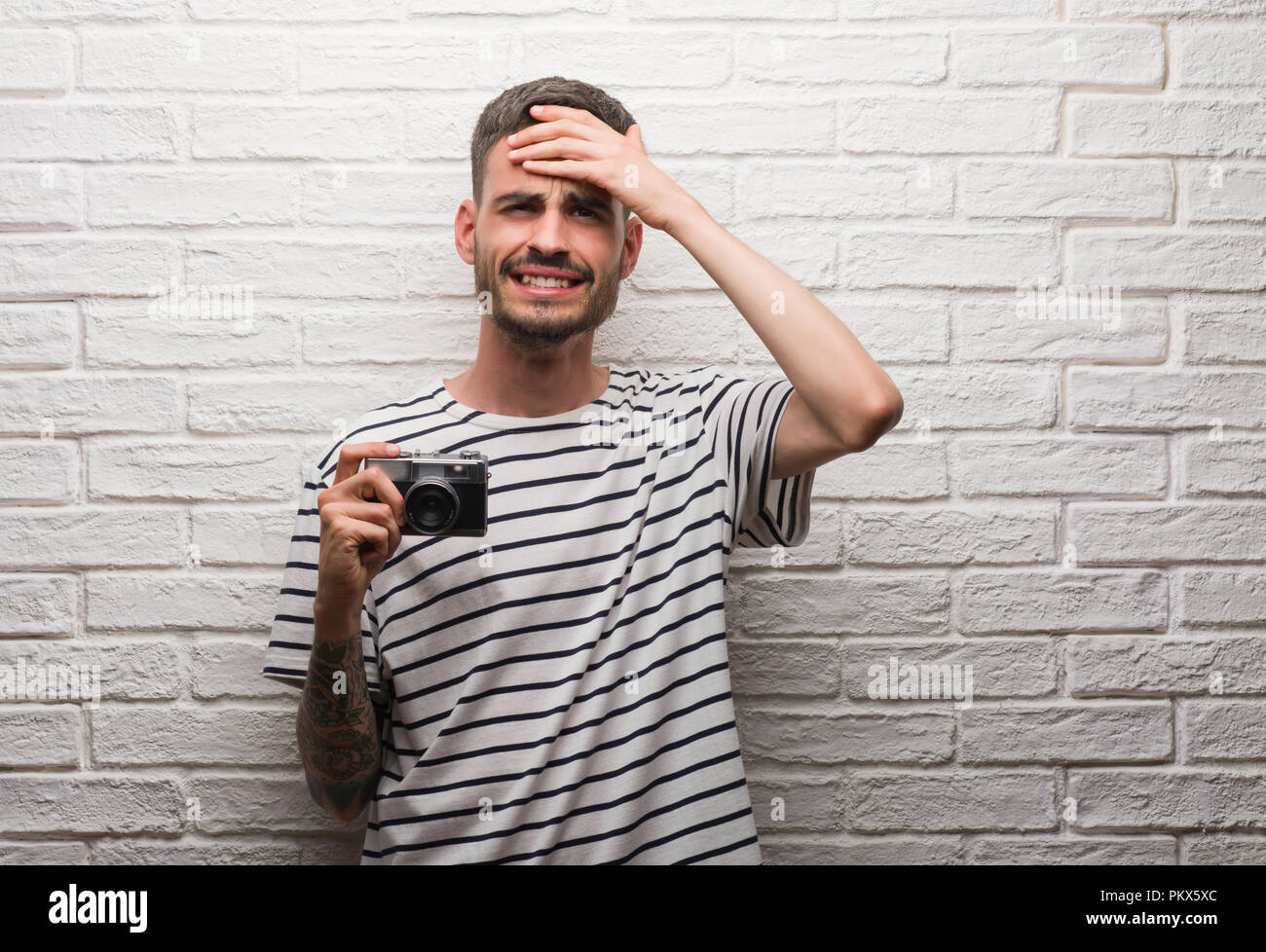 Young man holding vintage camera standing over white brick wall ...
