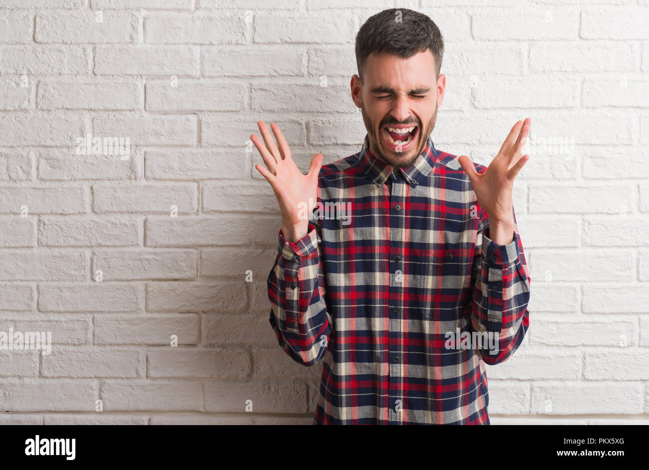 Young adult man standing over white brick wall celebrating mad and ...