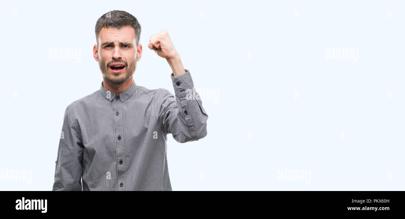 Young hipster man angry and mad raising fist frustrated and furious ...