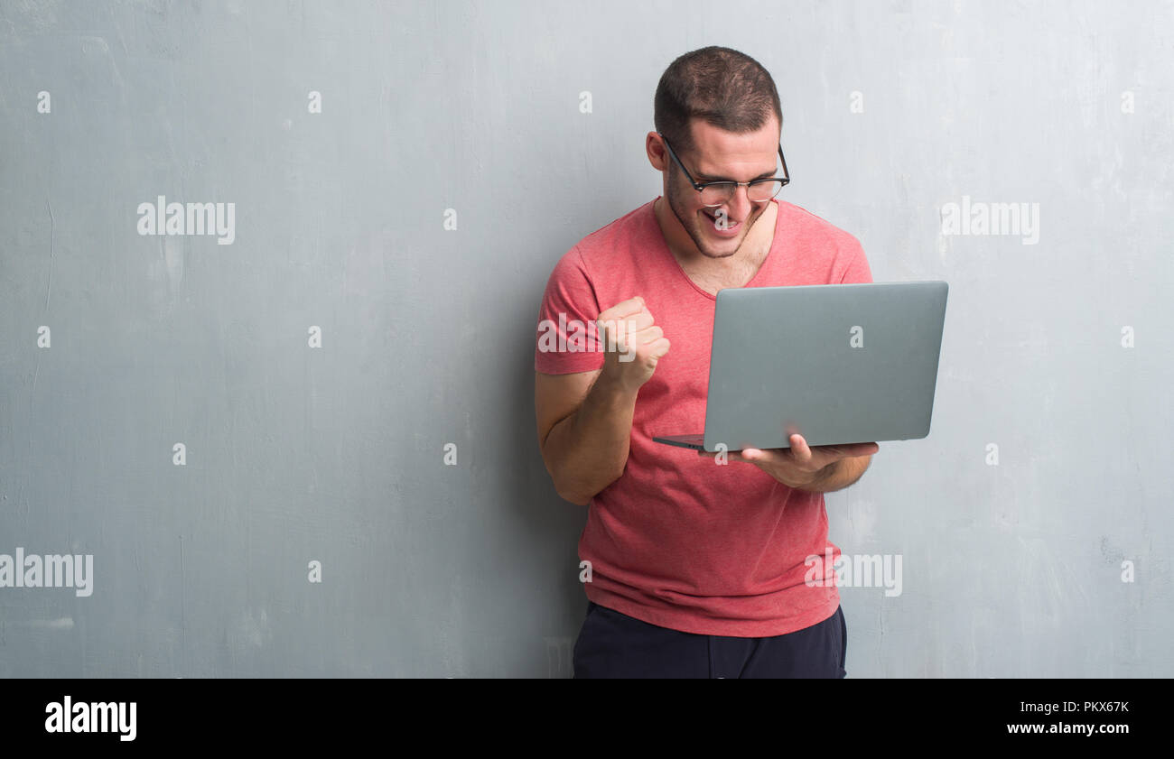 Young caucasian man over grey grunge wall using computer laptop ...