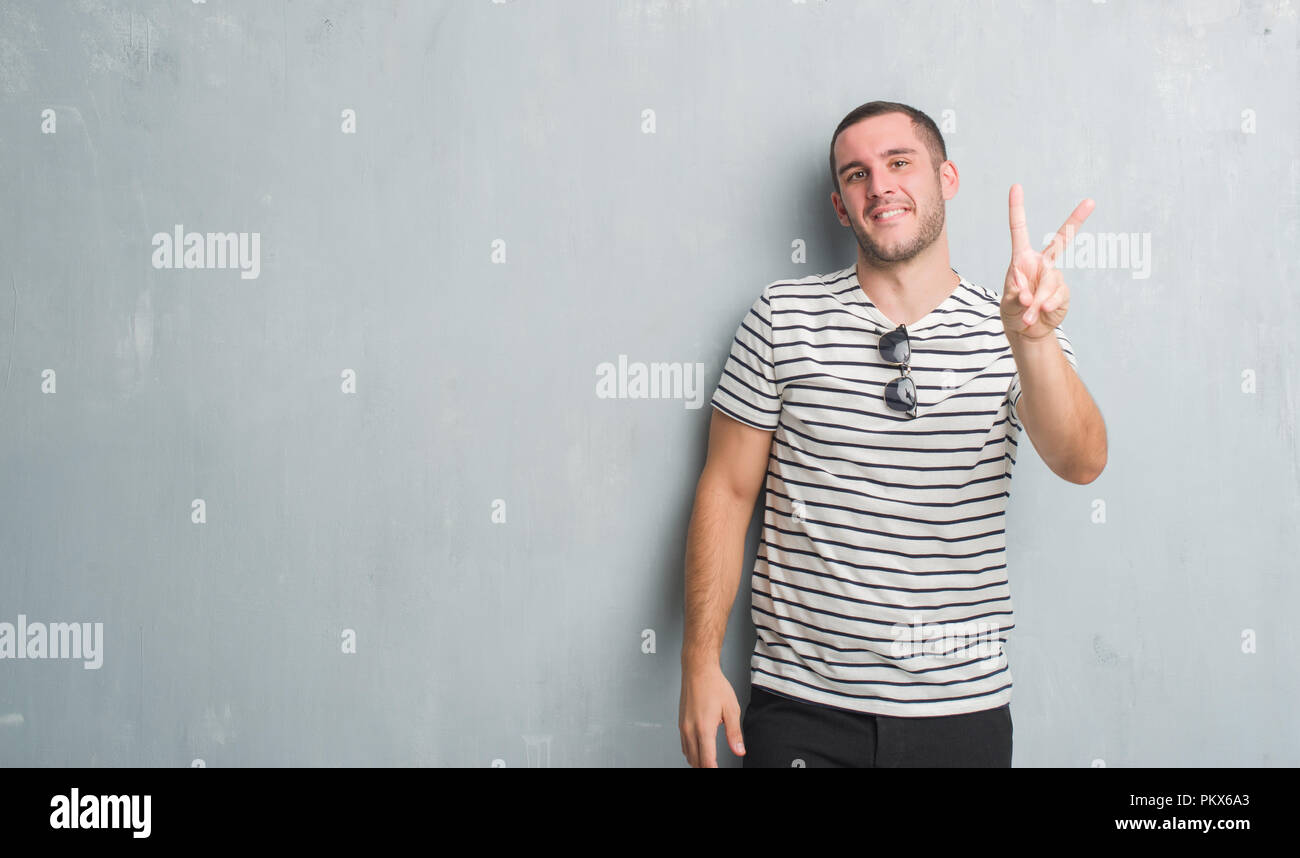Young caucasian man over grey grunge wall smiling looking to the camera ...