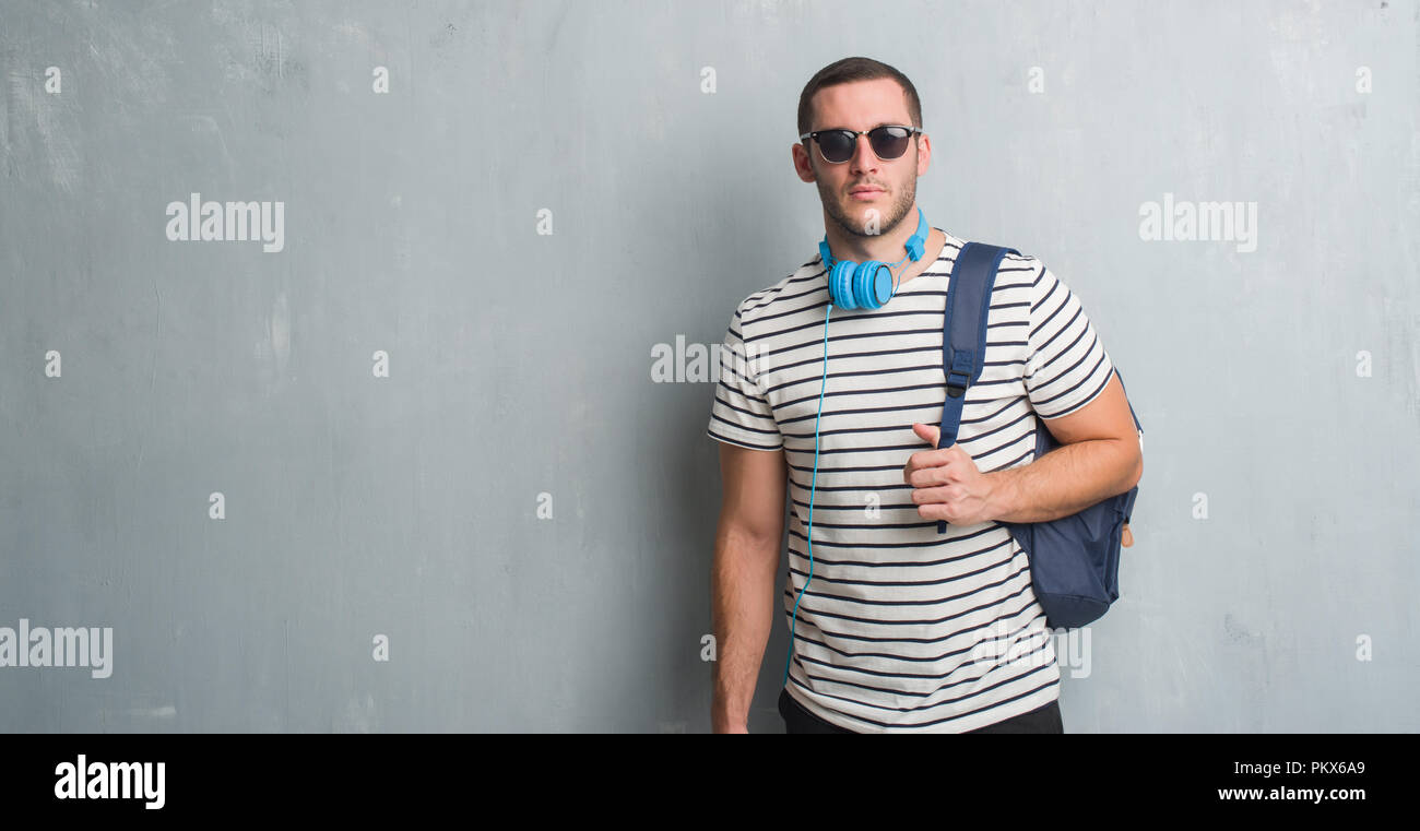 Young caucasian student man over grey grunge wall wearing headphones ...
