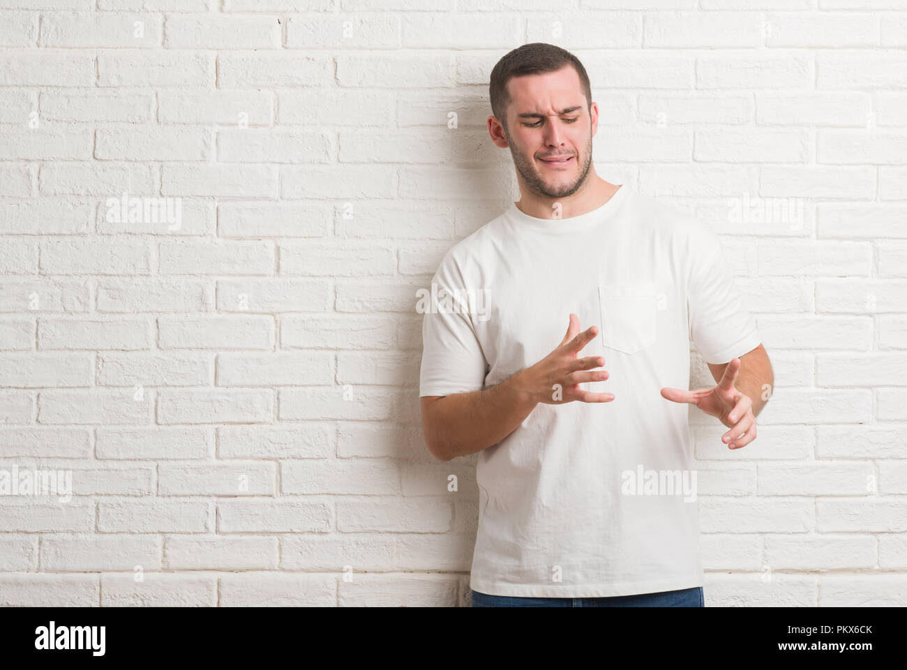 Young caucasian man standing over white brick wall angry and mad ...