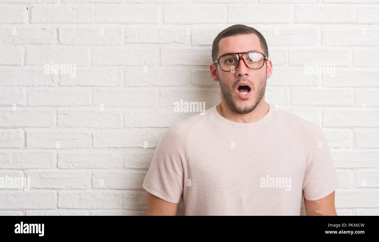 Young caucasian man standing over white brick wall wearing glasses ...