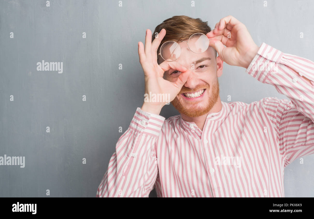 Young redhead man over grey grunge wall with happy face smiling doing ...