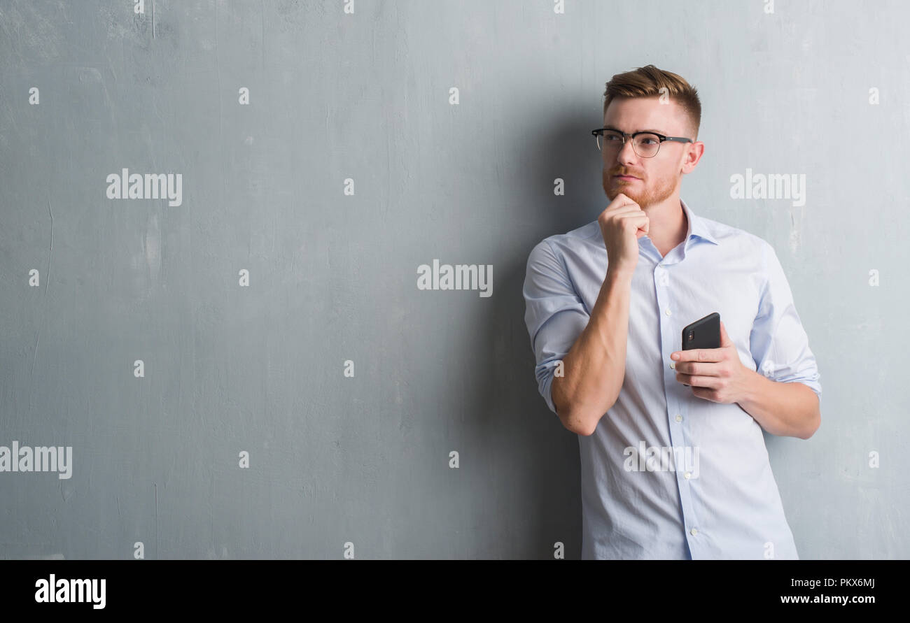 Young redhead man over grey grunge wall sending message using ...