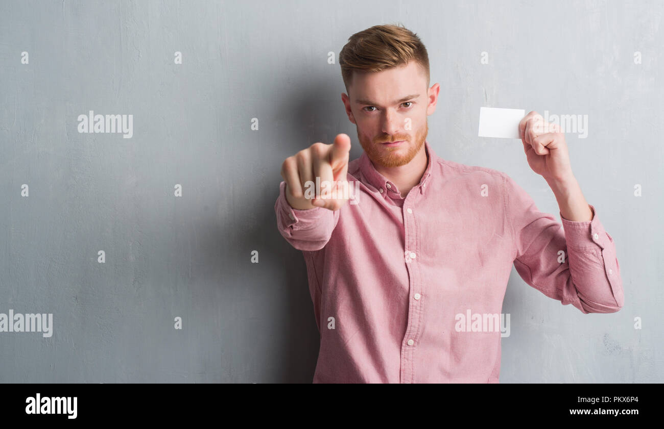 Young redhead man over grey grunge wall holding blank visit card ...