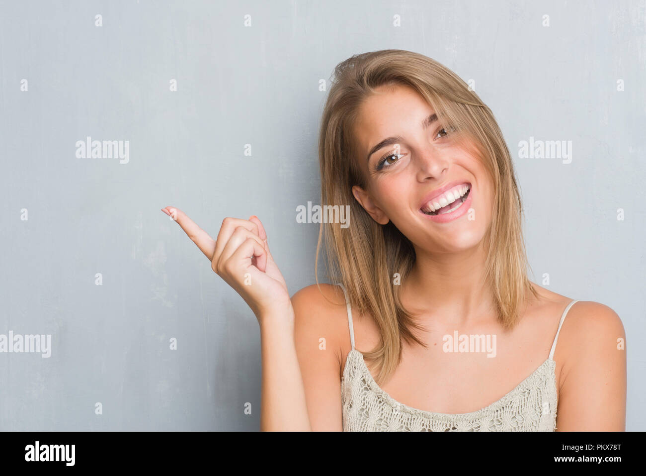 Beautiful young woman standing over grunge grey wall very happy ...