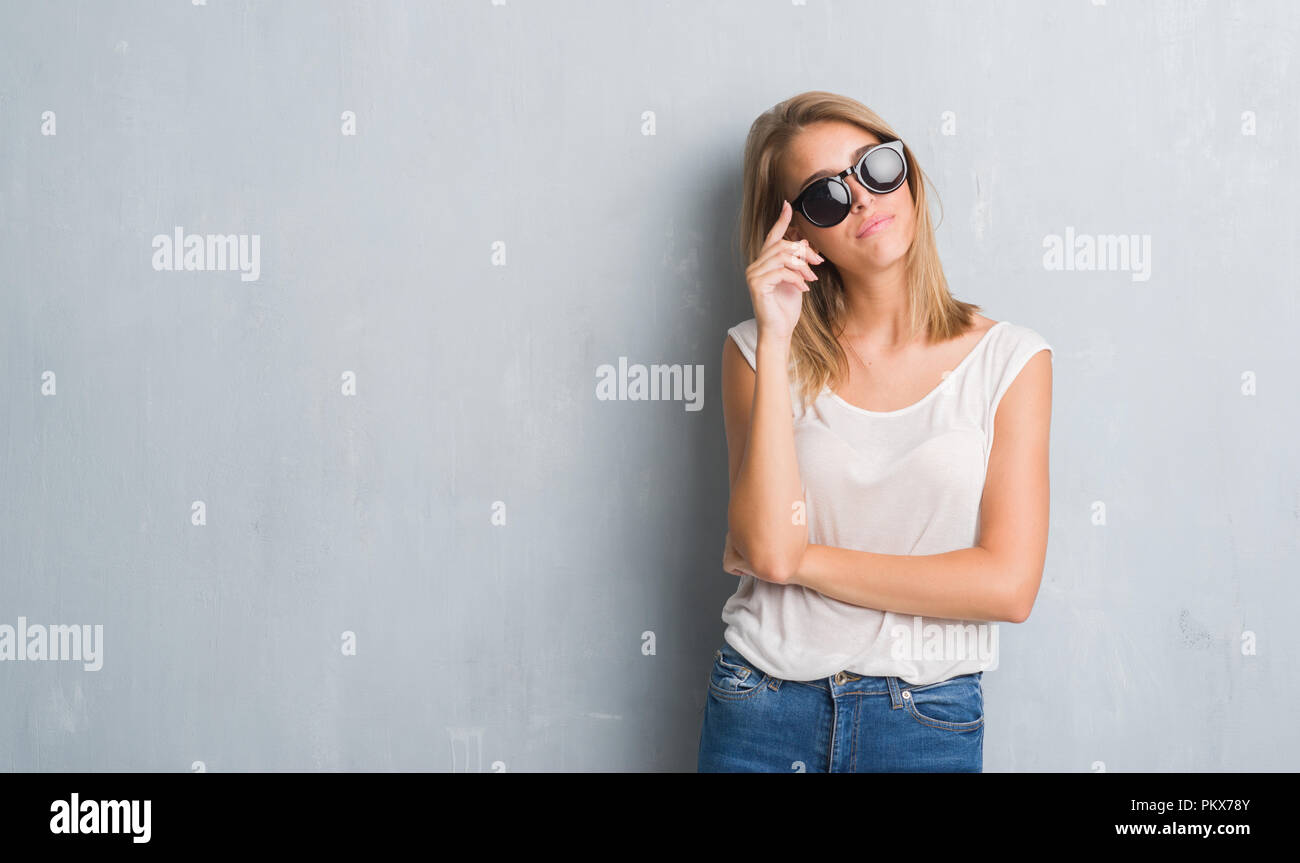 Beautiful young woman standing over grunge grey wall wearing fashion ...