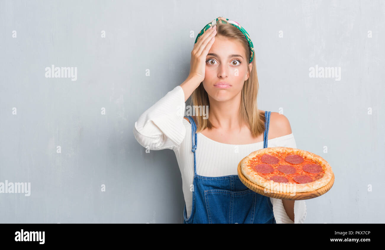 Beautiful young woman over grunge grey wall eating pepperoni pizza ...