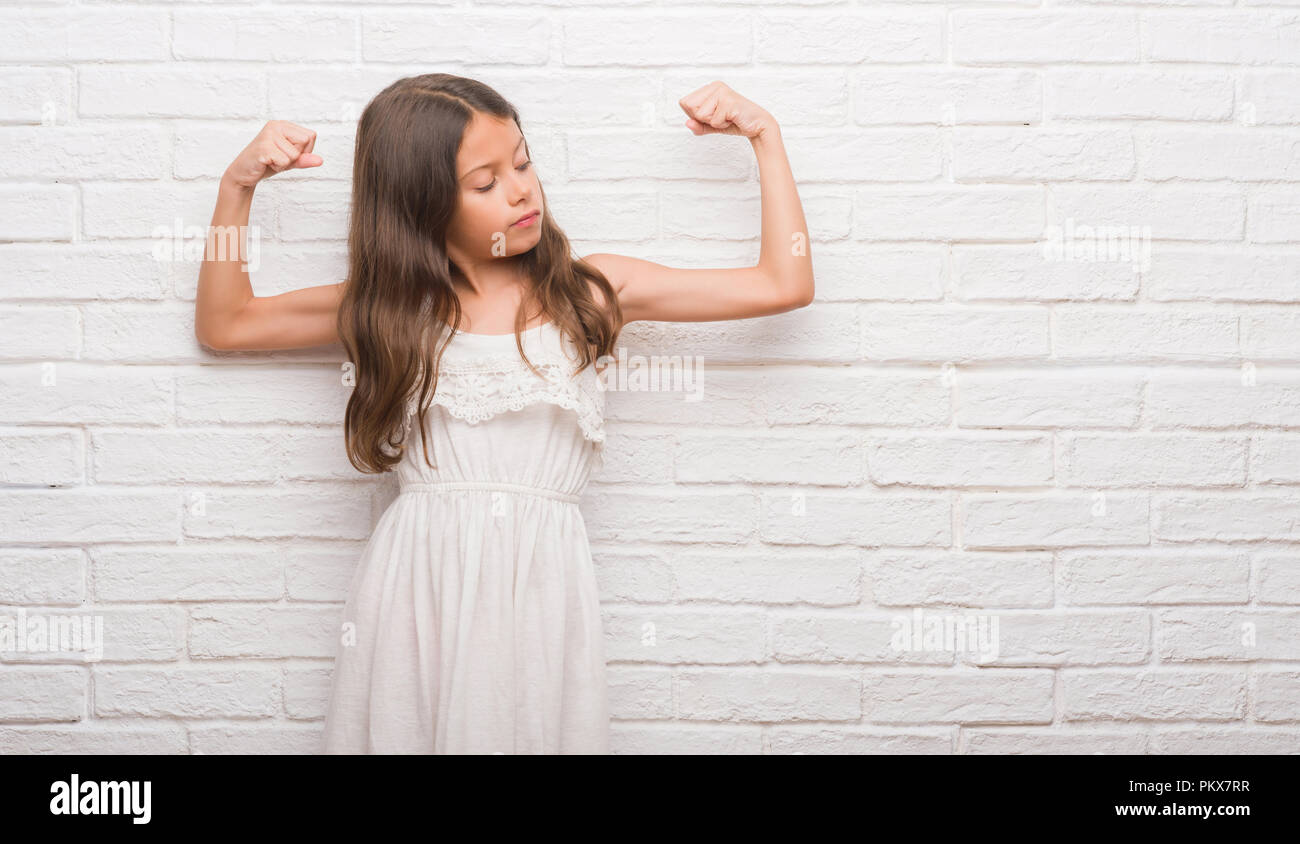 Young hispanic kid over white brick wall showing arms muscles smiling ...