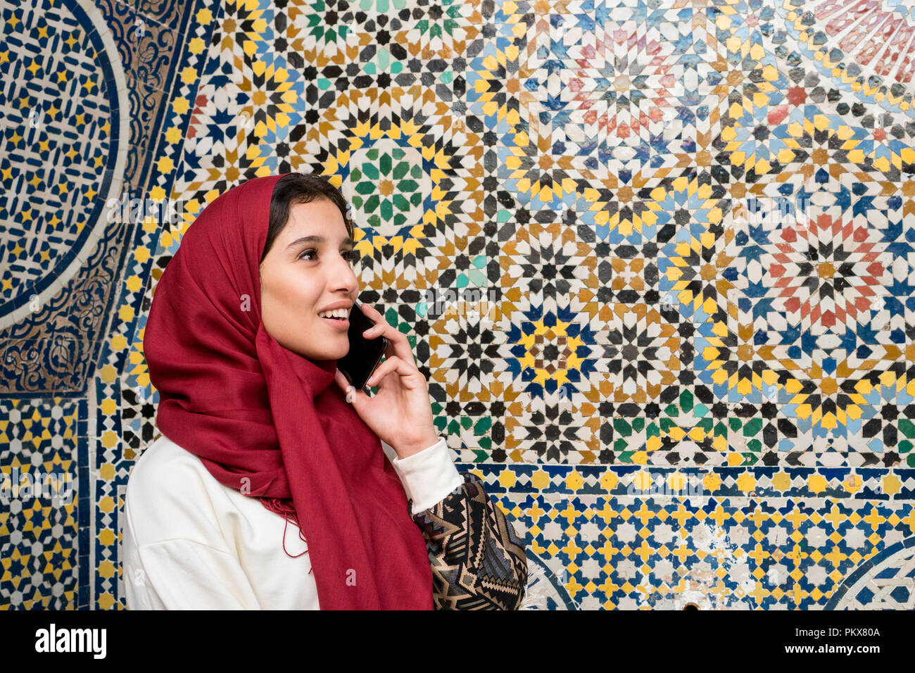 Portrait of young muslim woman with red hijab talking over smart phone ...