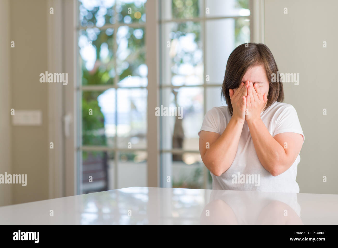 Down syndrome woman at home with sad expression covering face with ...