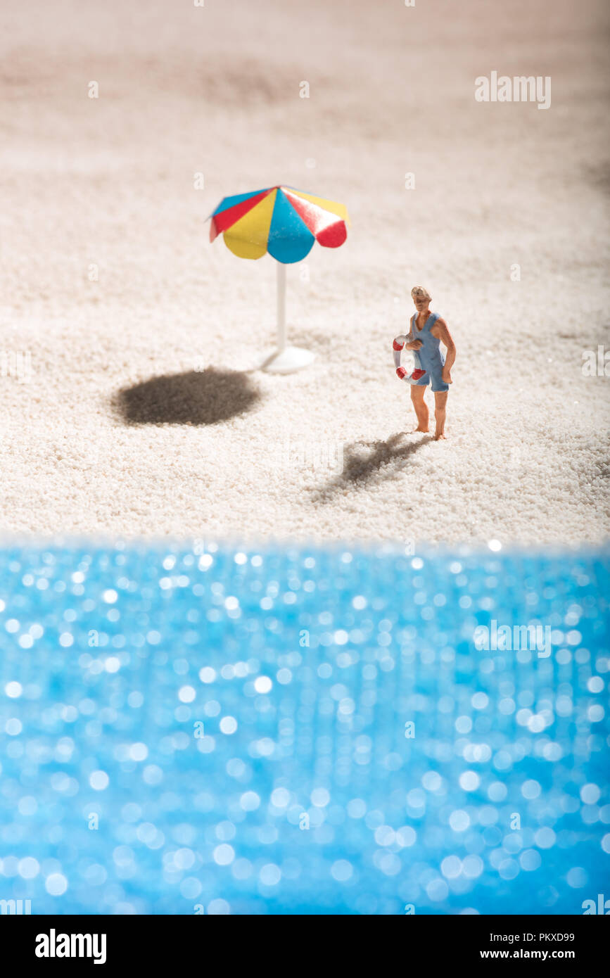 Miniature people lifeguard figure walking across a sandy beach with ...