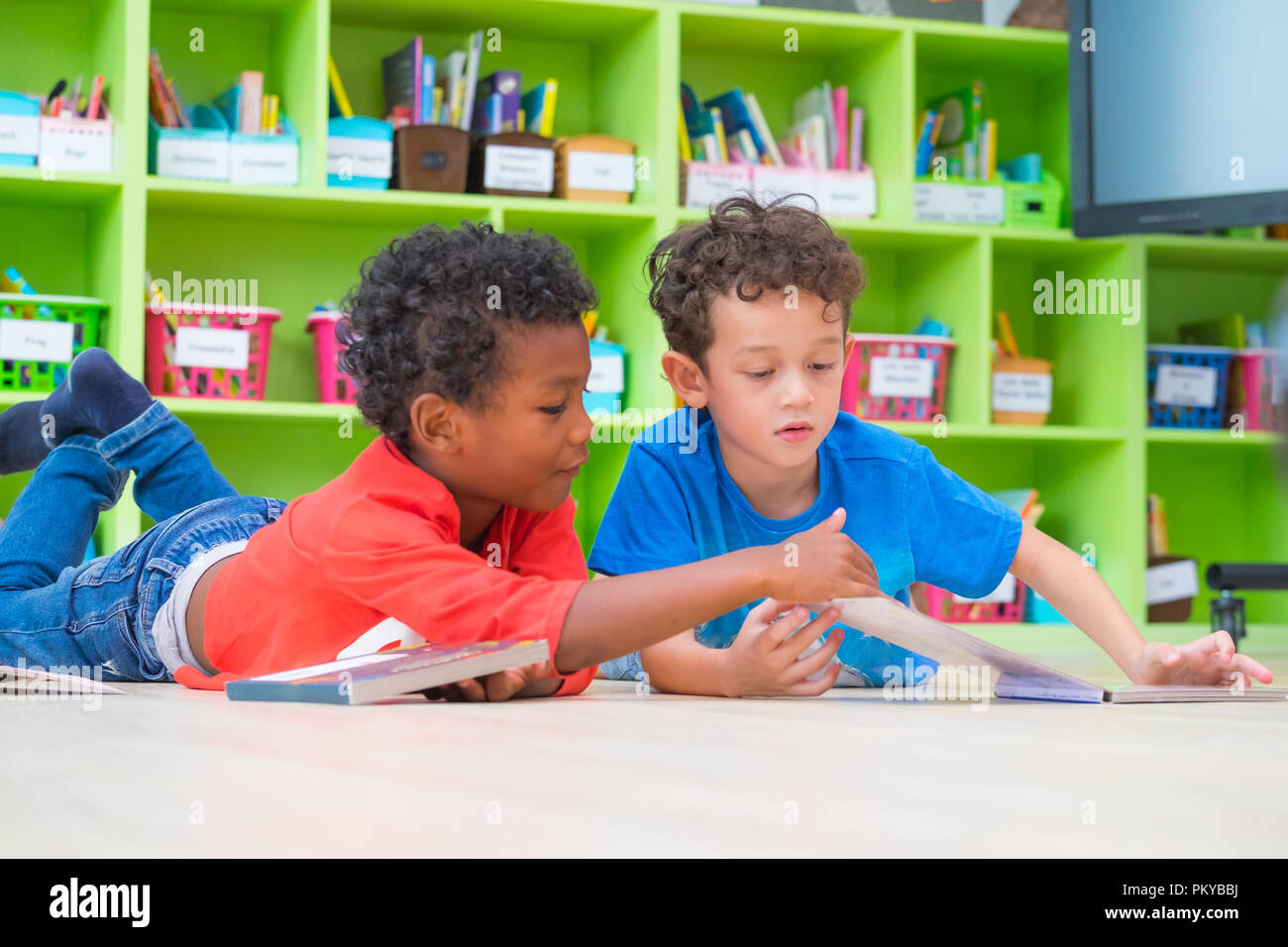 Two boy kid lay down on floor and reading tale book in preschool ...