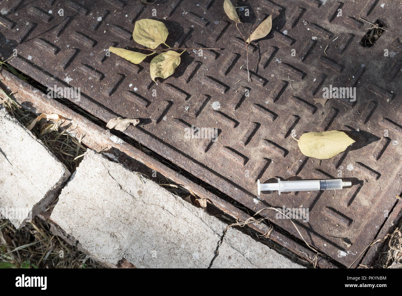 Discarded empty syringe outdoors on broken drain - Drug abuse concept ...