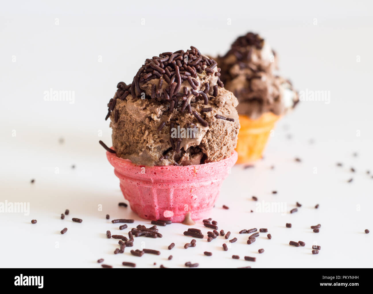 Ice cream in small pink wafer cup on white with chocolate sprinkles ...