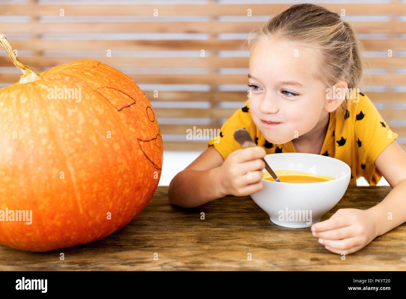 Cute little girl eating pumpkin soup and looking at a large Halloween ...