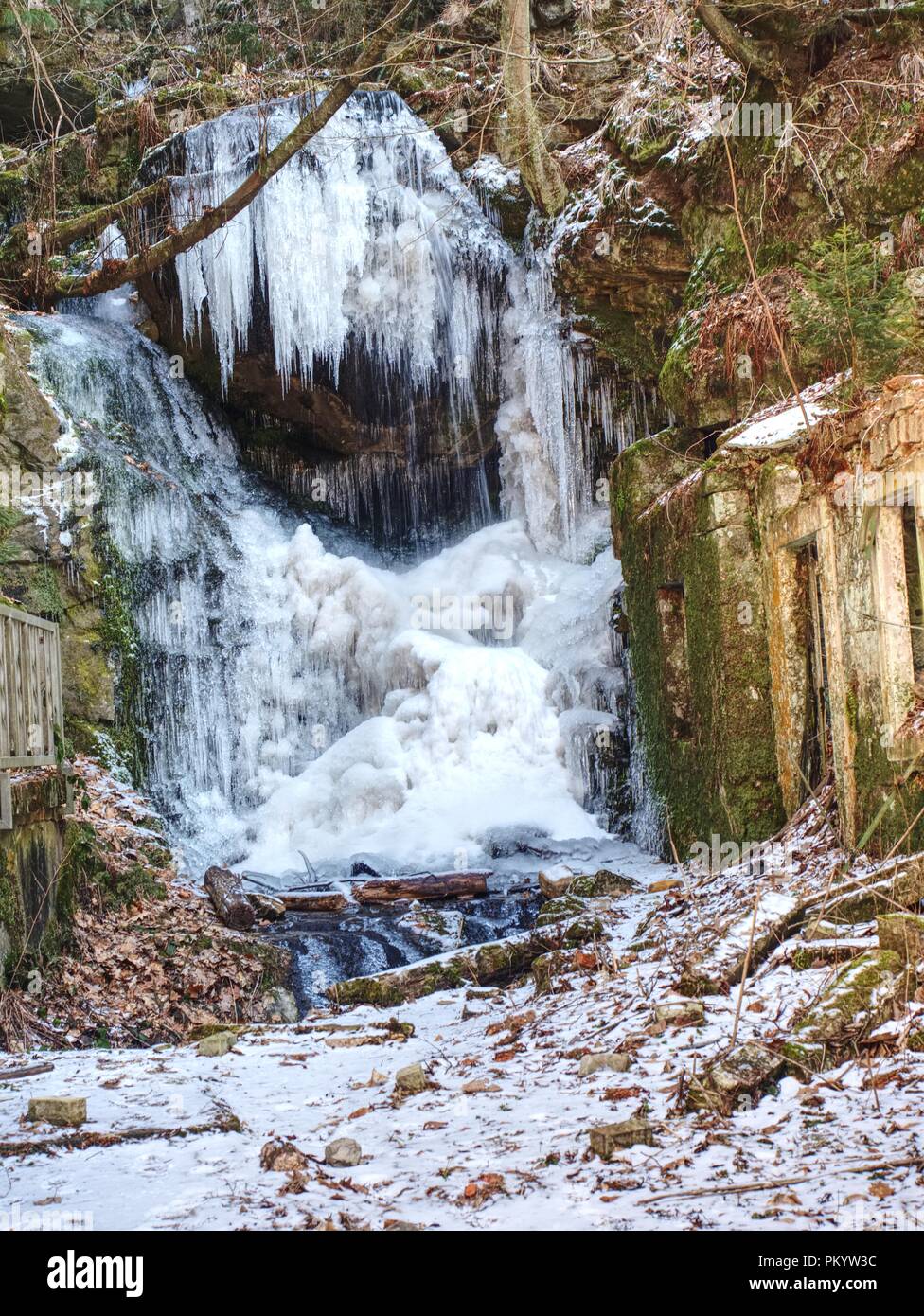 Winter frozen waterfall. Small pond and snowy boulders bellow cascade ...