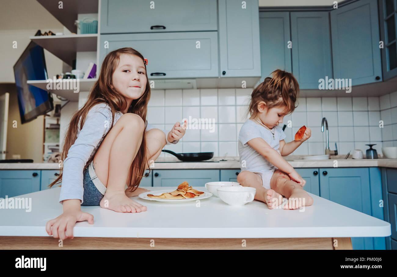 Two little girls in the kitchen sitting on the table Stock Photo - Alamy