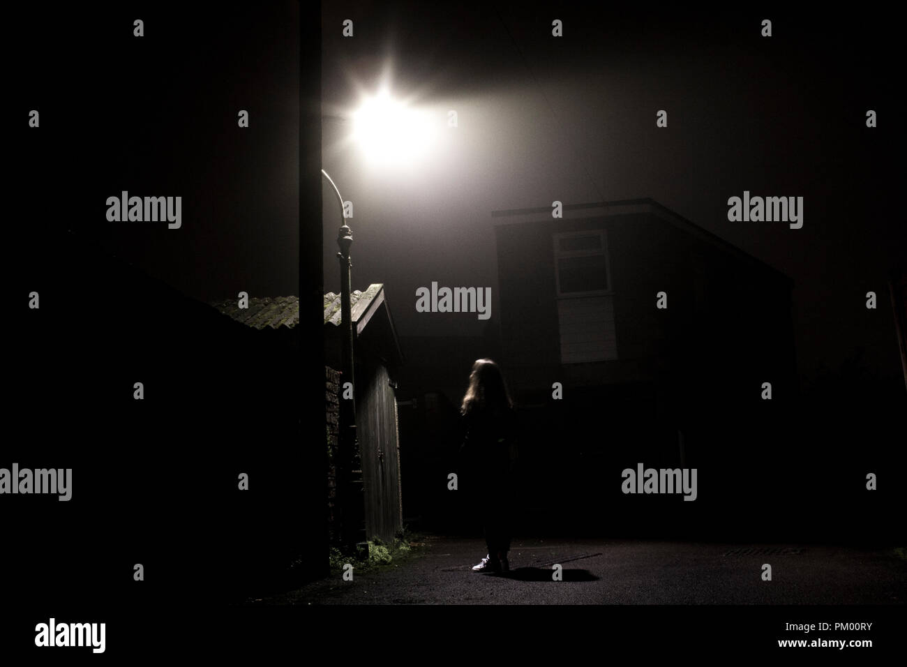 Girl in the night standing under a lamp post Stock Photo - Alamy
