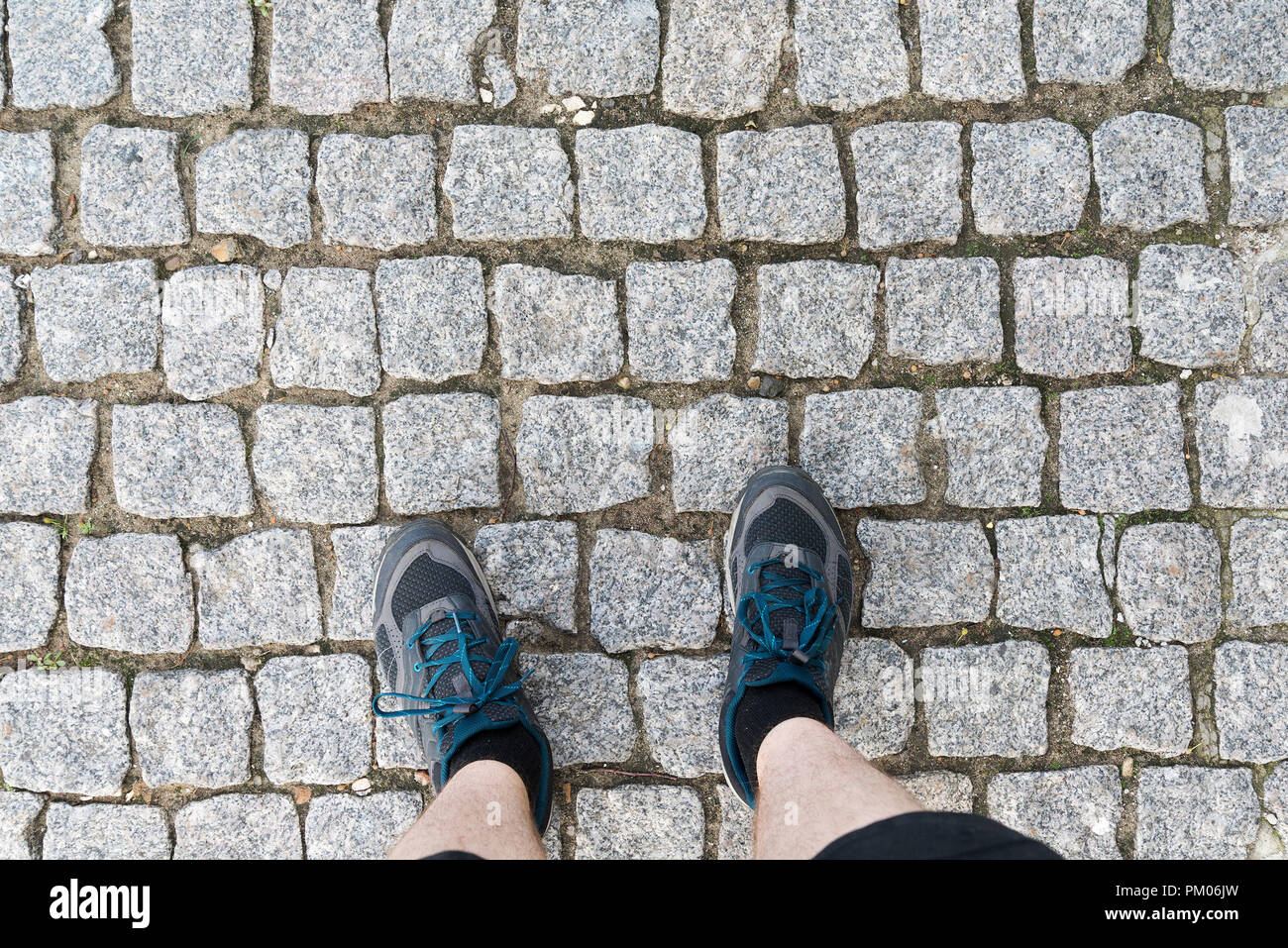 Top view, feet on the pavement in sneakers. The old cobblestones of the ...