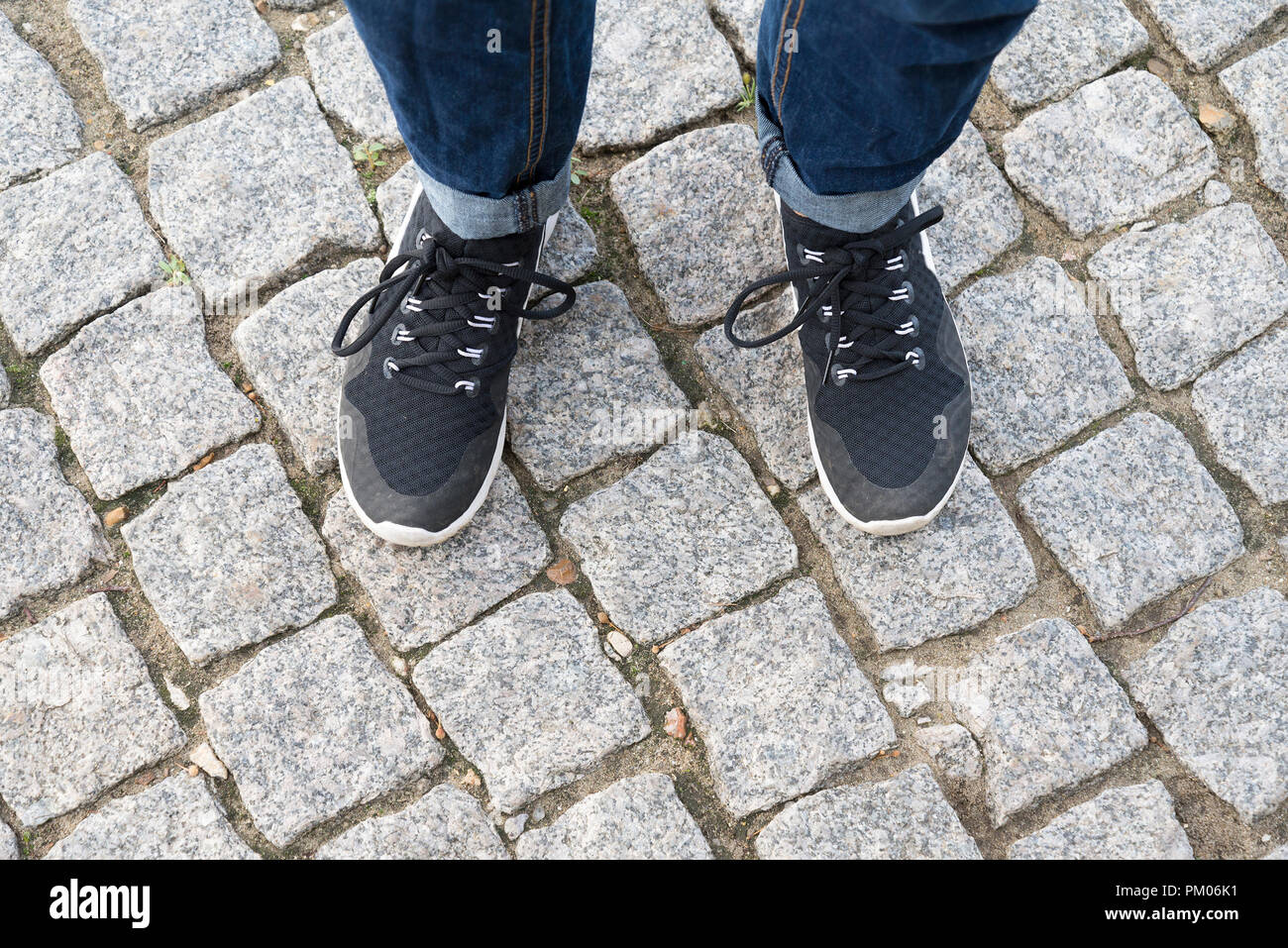 Top view, feet on the pavement in sneakers. The old cobblestones of the ...
