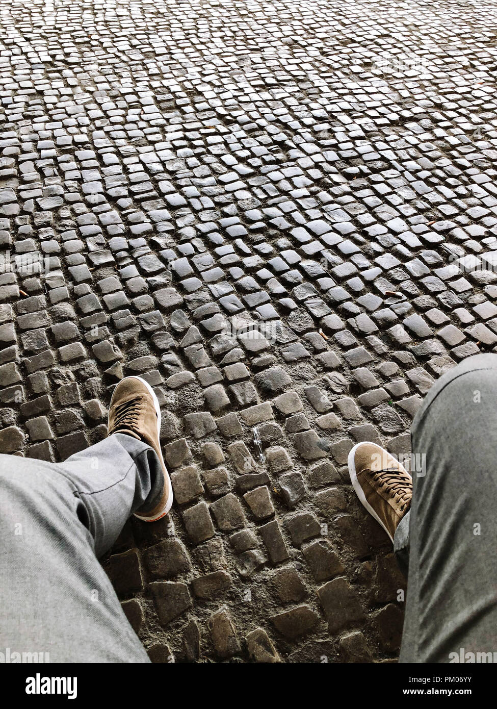 Legs of business casual young man sitting over a cobblestone pavement ...