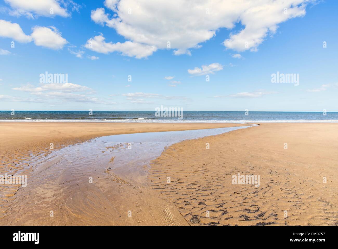 A wide stretch of water narrows as it runs to the sea across the beach ...