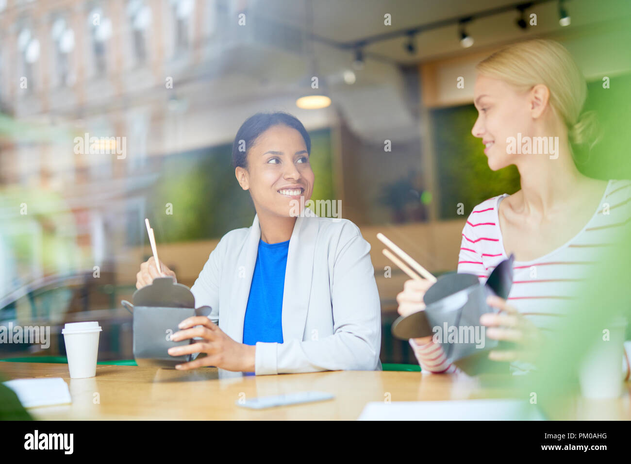 Two young colleagues chatting at lunch break while having chinese ...