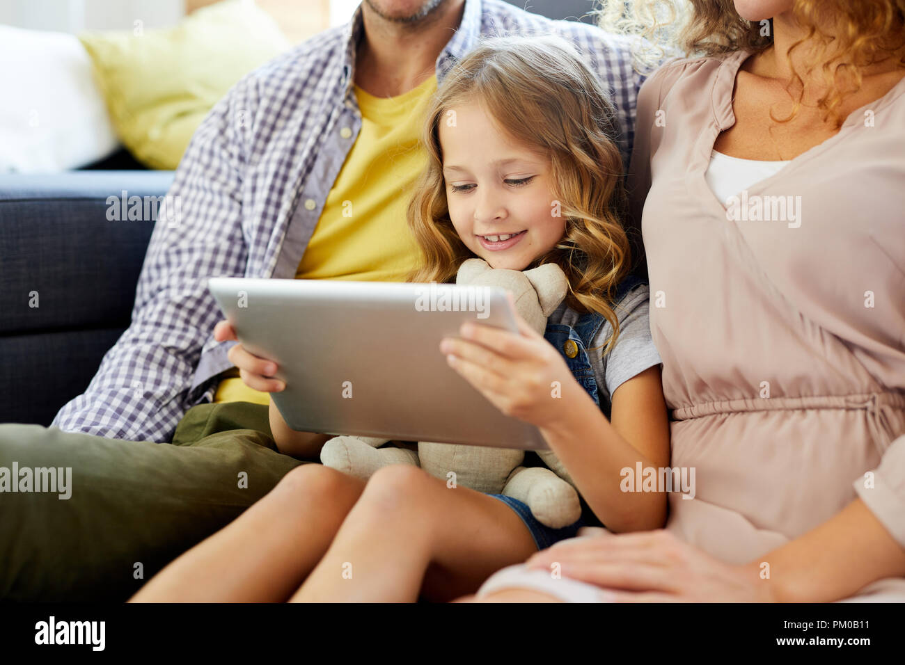 Cute happy child watching curious video in touchpad with her parents ...