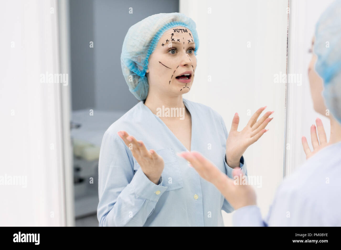 Confused female in whitecoat standing in front of mirror and looking at ...