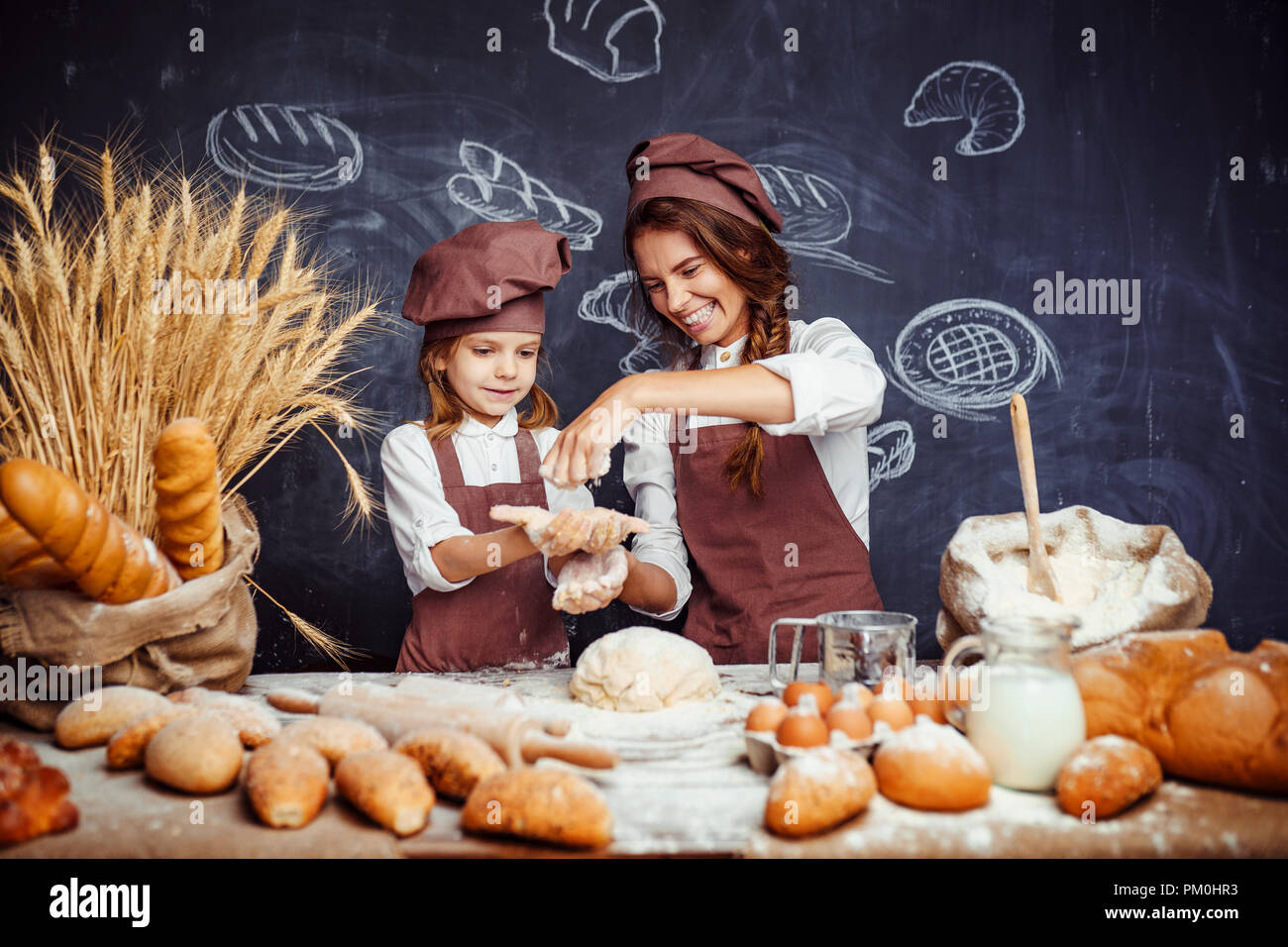 Woman with little girl in hats and aprons making pastries from dough ...