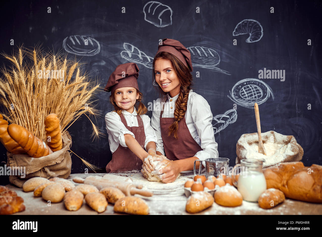 Woman with little girl in hats and aprons making pastries from dough ...