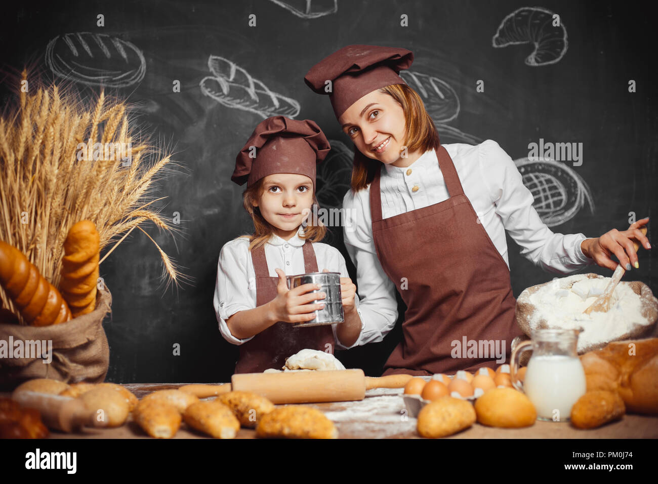 Woman with little girl in hats and aprons making pastries from dough ...