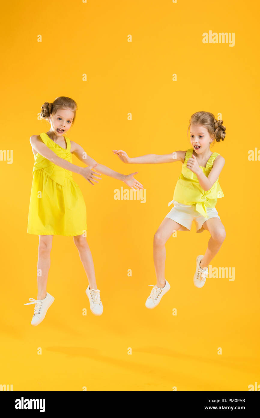 The girls of the twins are dancing together on a yellow background ...