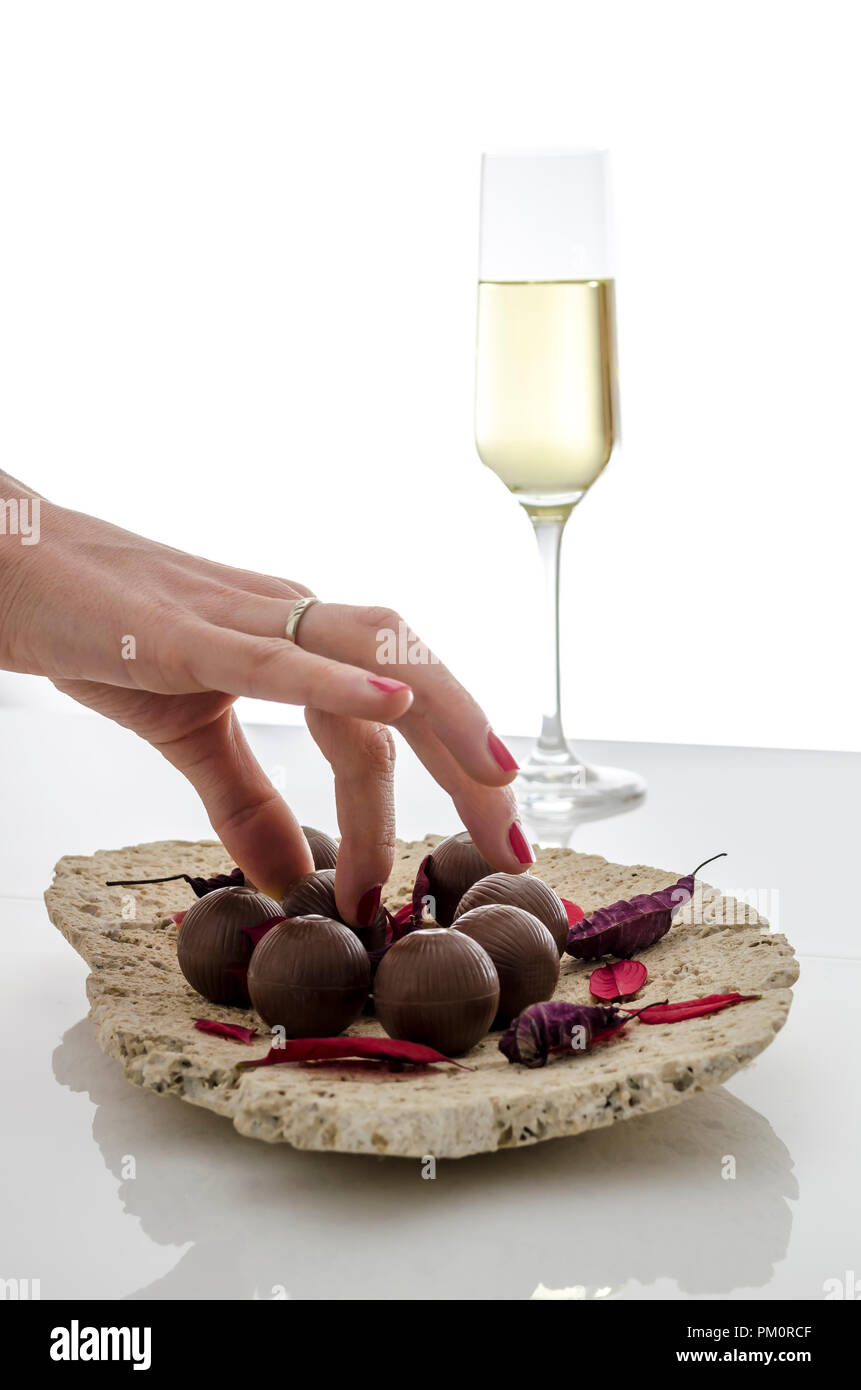 Female hand taking a chocolate candy from a plate on a white table ...