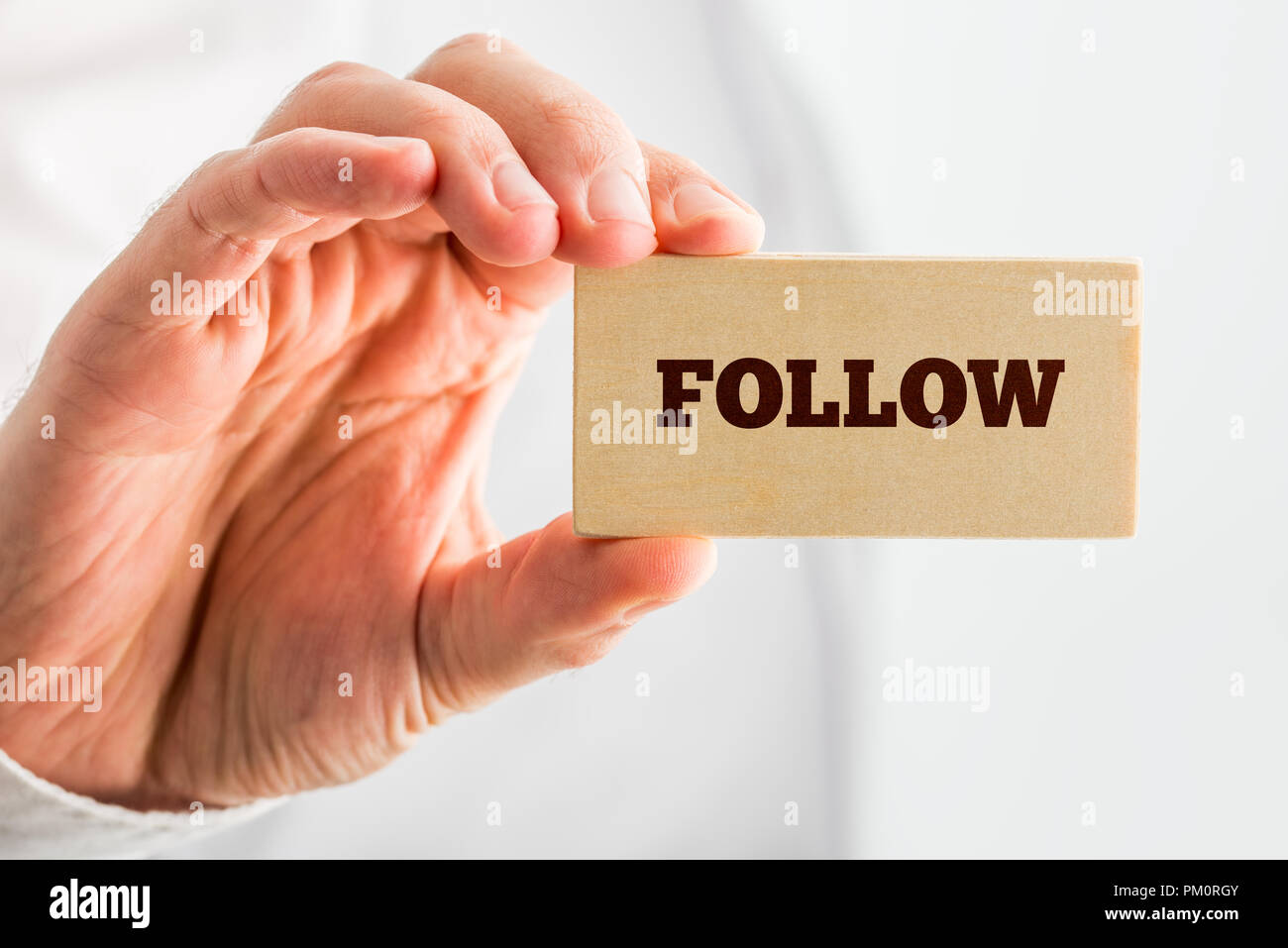 Human hand holding small piece wood showing Follow text over his white ...